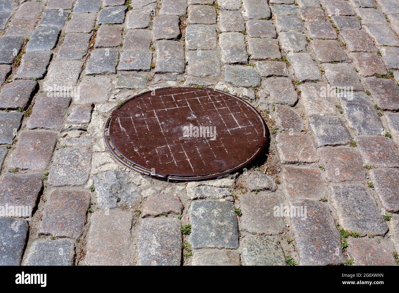 iron rusty manhole cover on an old cobblestone road on a sunny day on ...