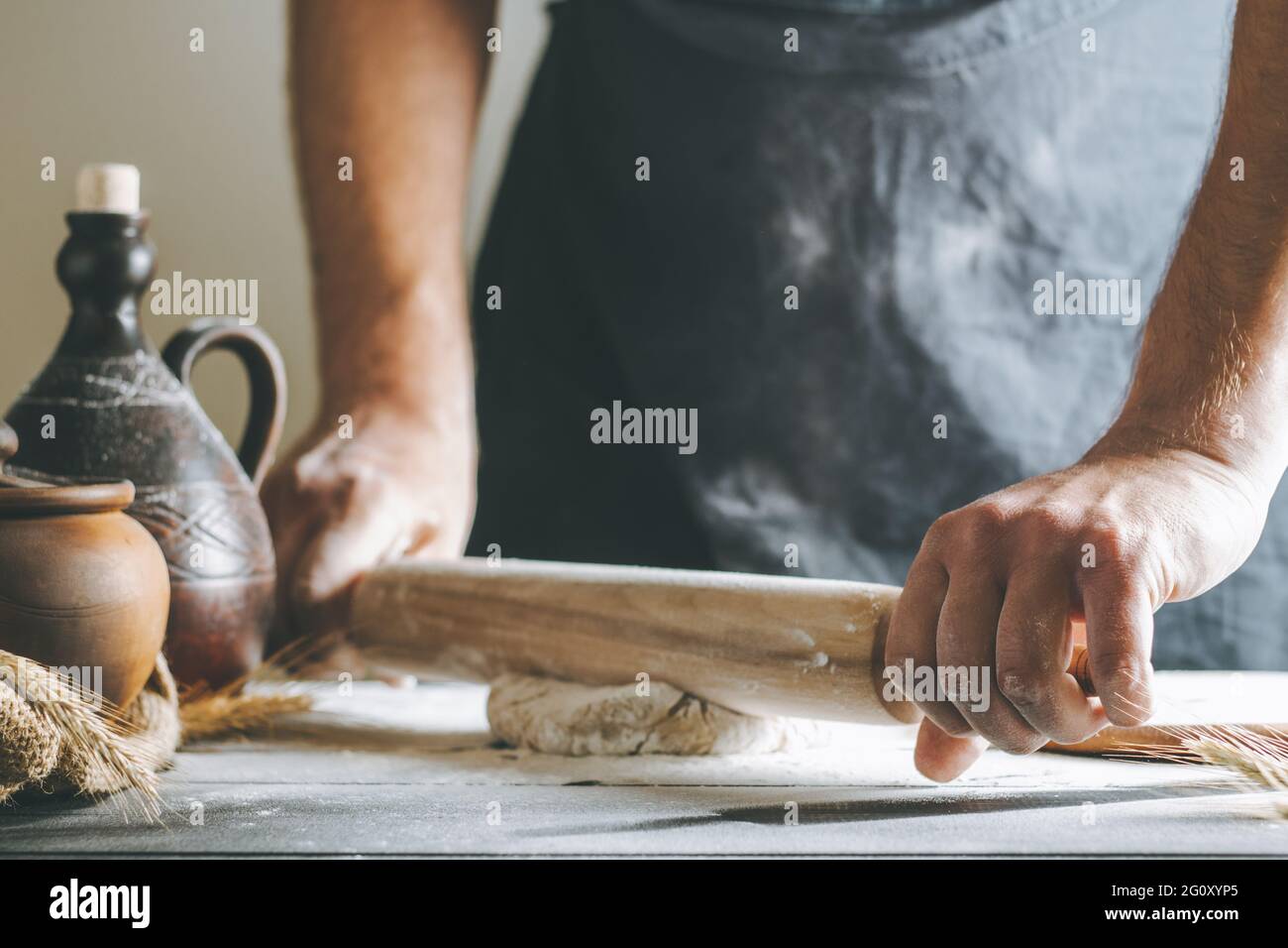 Male hands roll dough and flour with rolling pin next to clay pot and ...