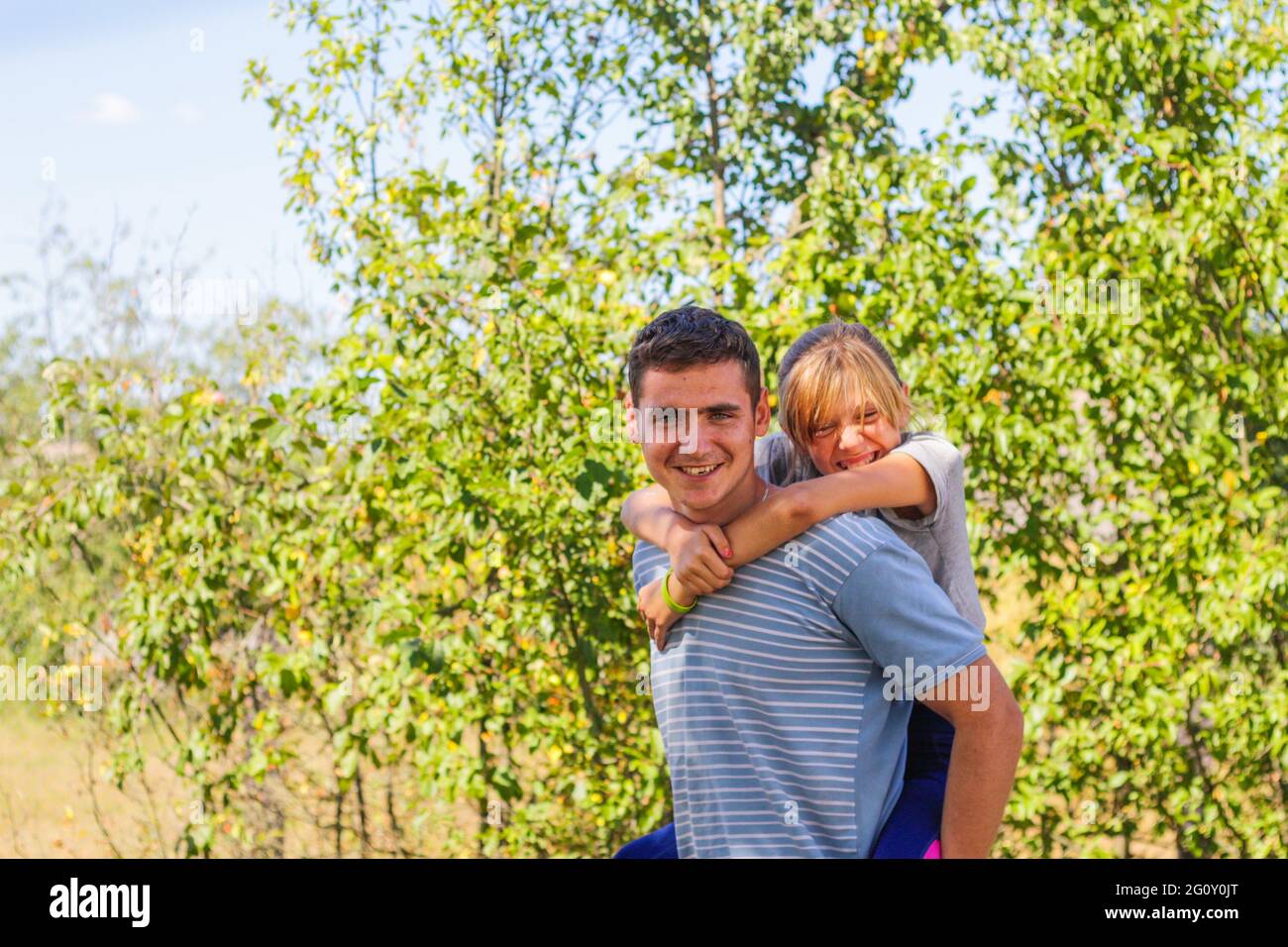 Defocused brother giving sister ride on back. Portrait of happy girl on ...