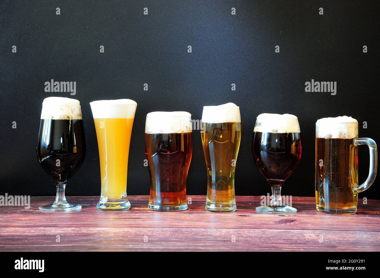 Six glasses of different types of beer are in a row on a wooden table ...