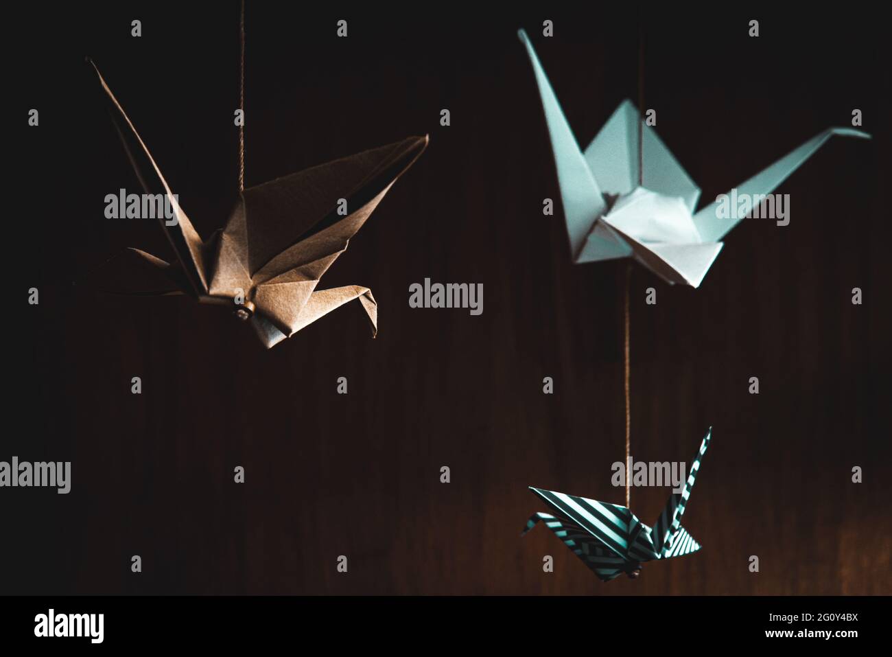 Three origami swans hanging from the roof with a wooden background ...