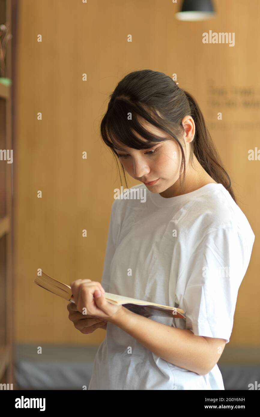 Portrait of young female student reading a book while searching book ...
