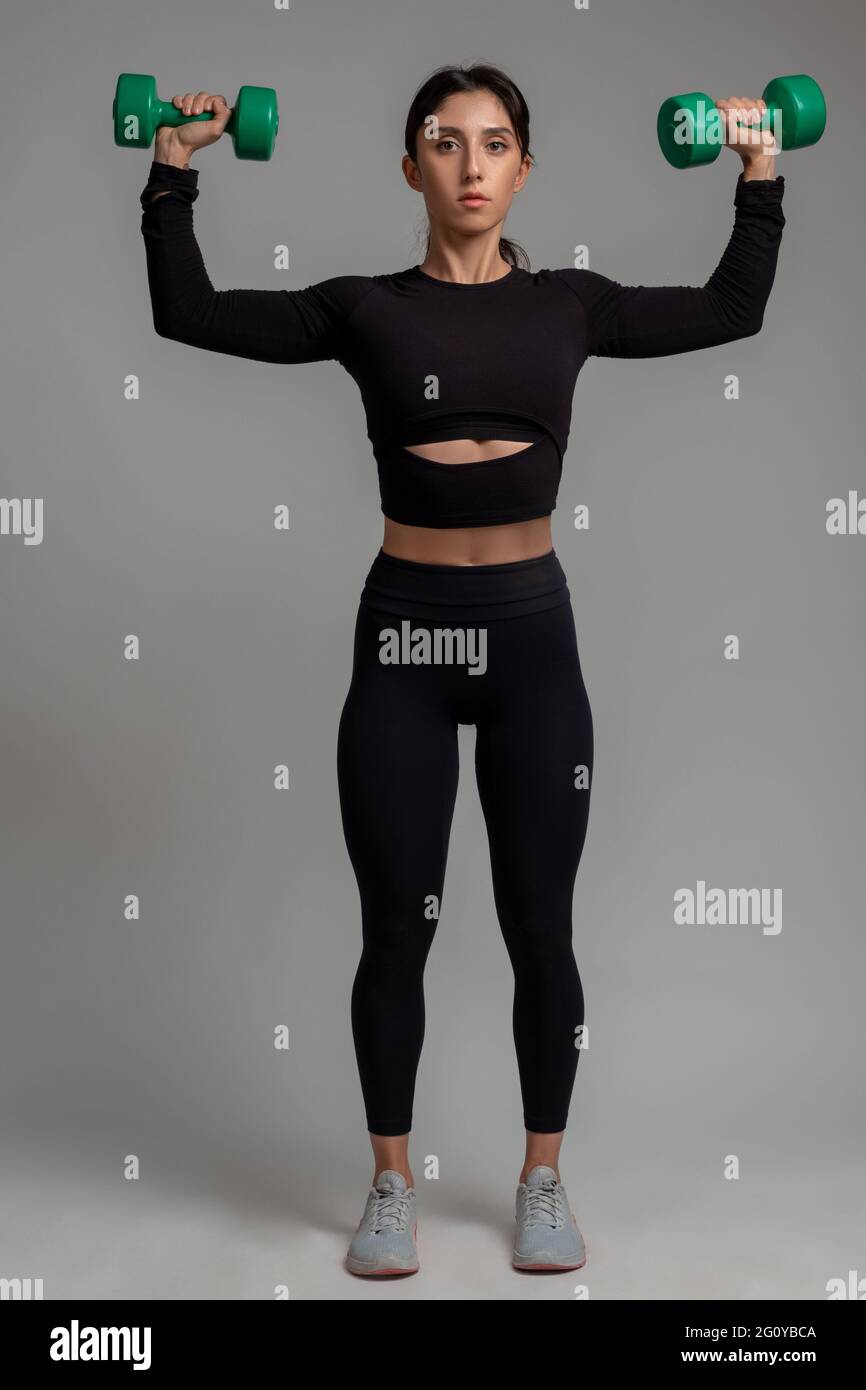 Fit brunette doing dumbbell shoulder press on grey background Stock ...