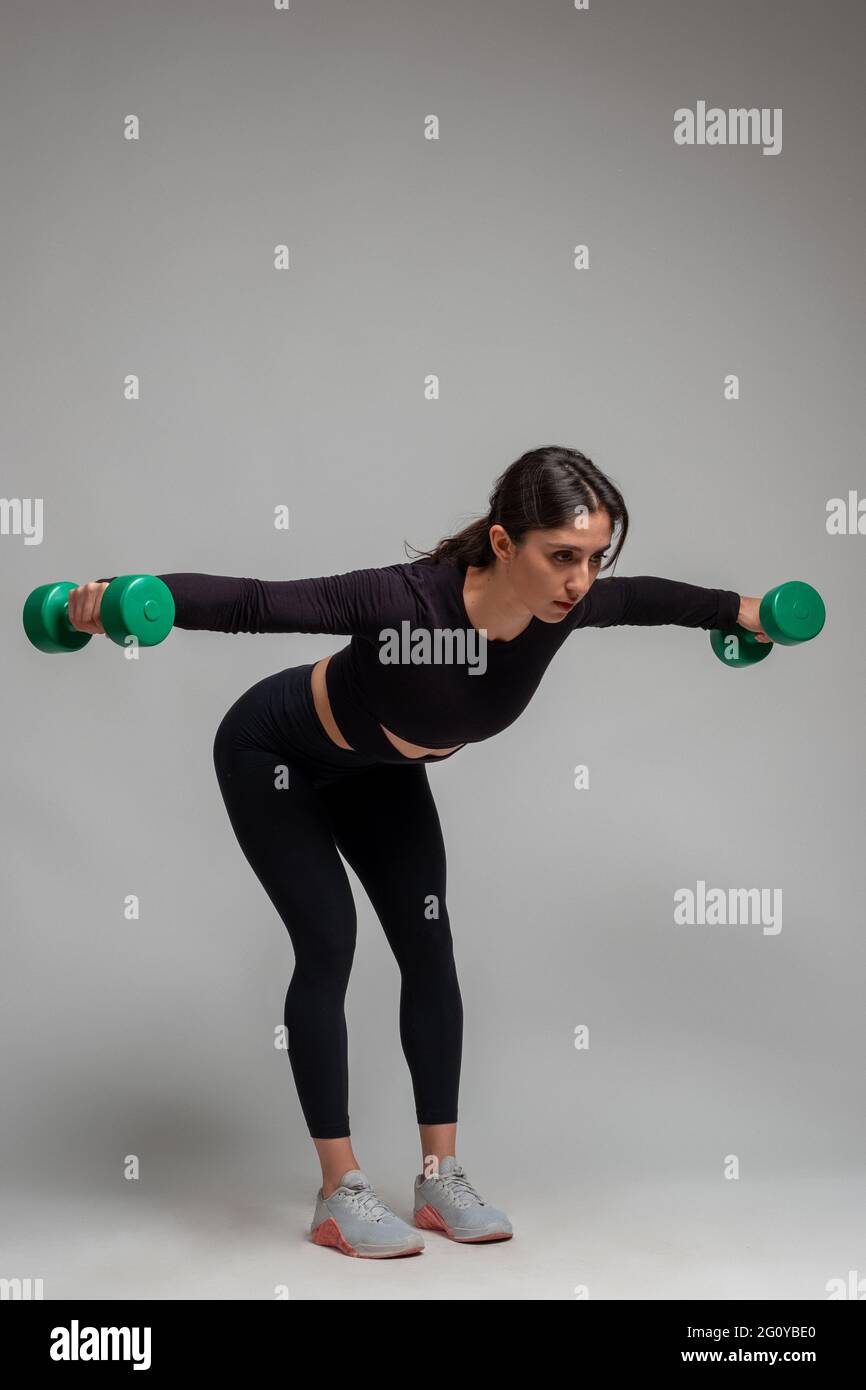 Athletic girl doing shoulders exercises with dumbbells on grey ...