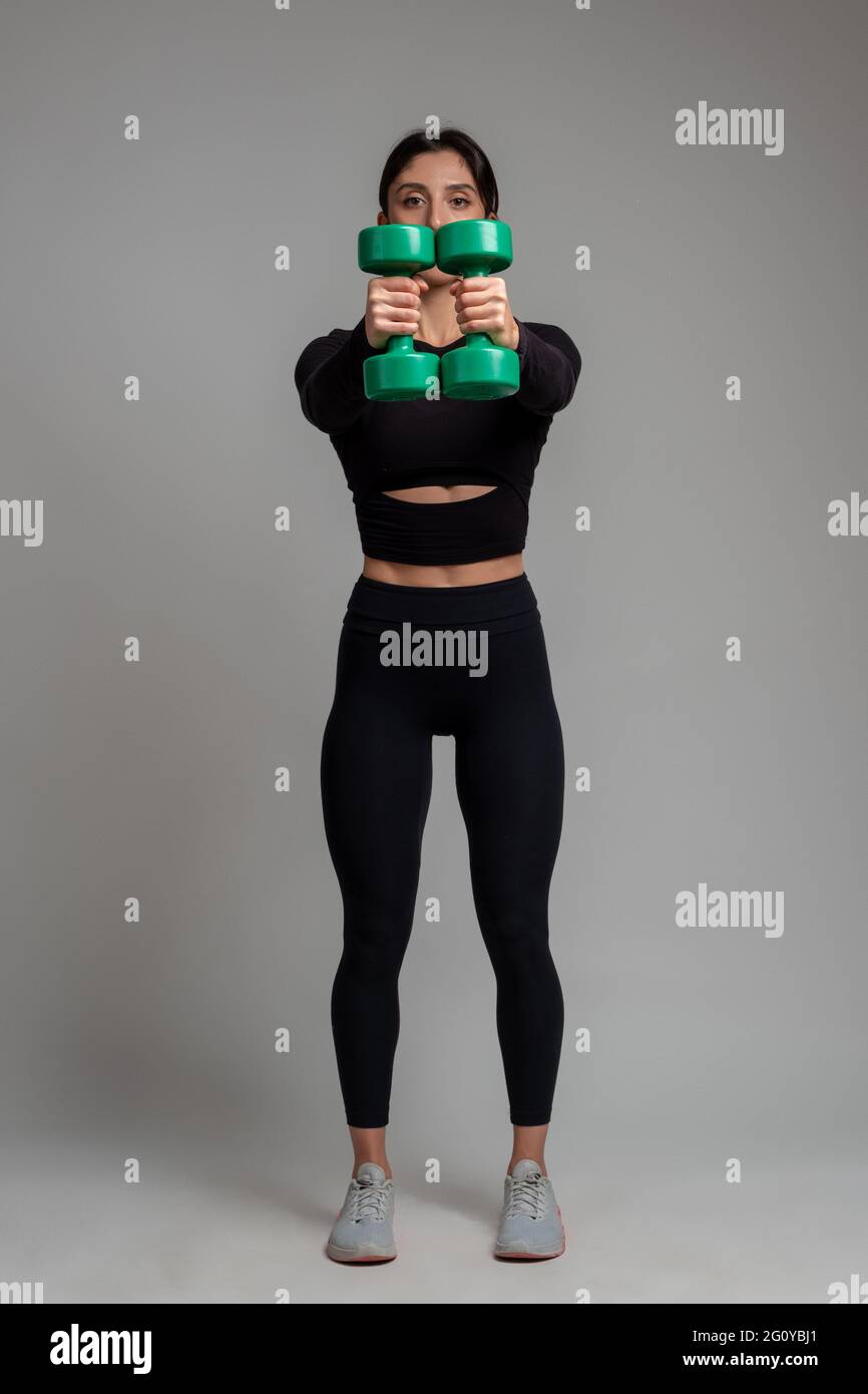 Sporty girl performing shoulder exercises with dumbbells on grey ...