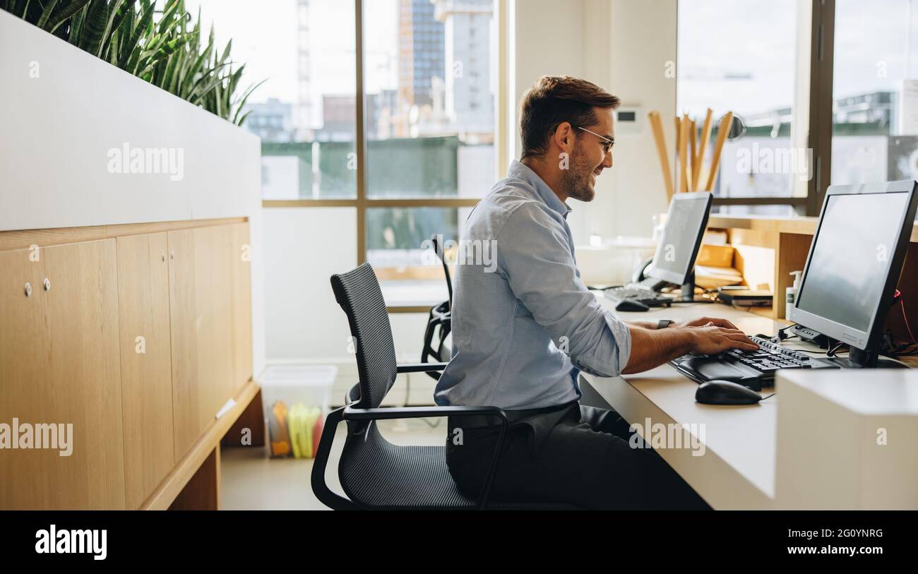 Manager smiling while working on computer. Happy young man sitting in ...