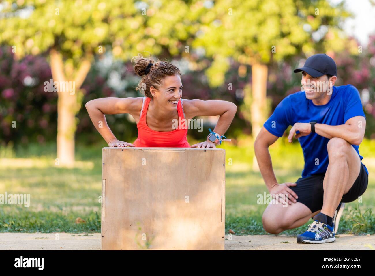 Happy woman doing push ups and working out in the park. The man is her ...