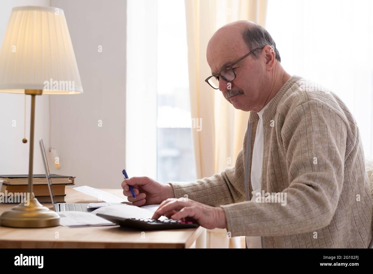 Senior man sitting with paperwork and using calculator while counting ...