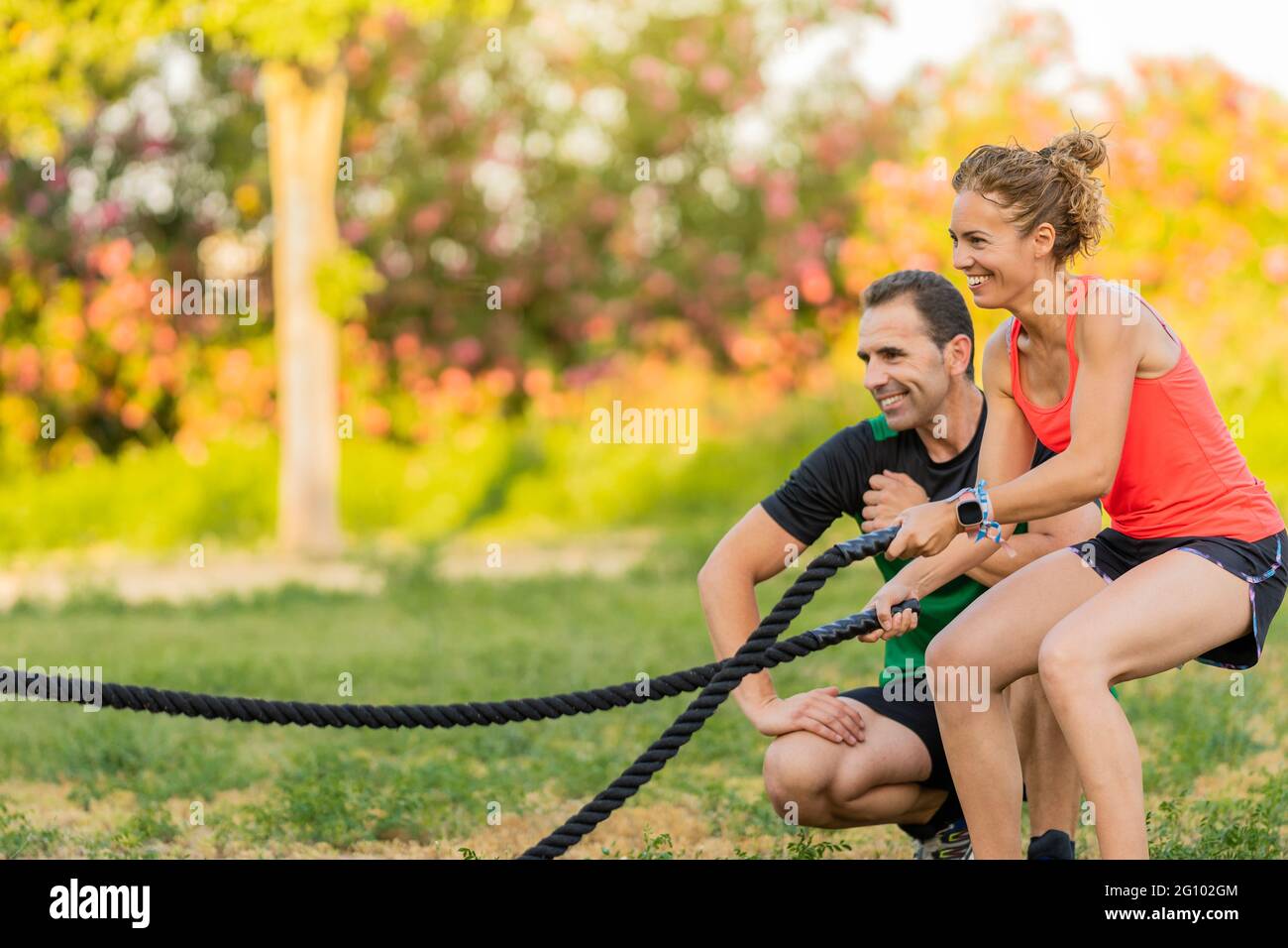 Smiley woman using a battle rope in the park and working out with her ...