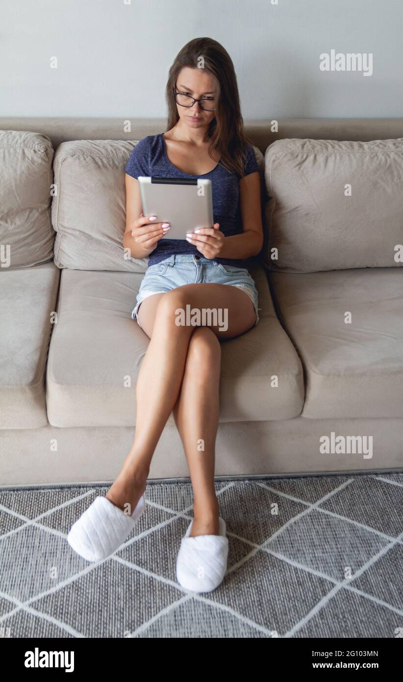 Young woman sitting on sofa and using tablet at home Stock Photo - Alamy