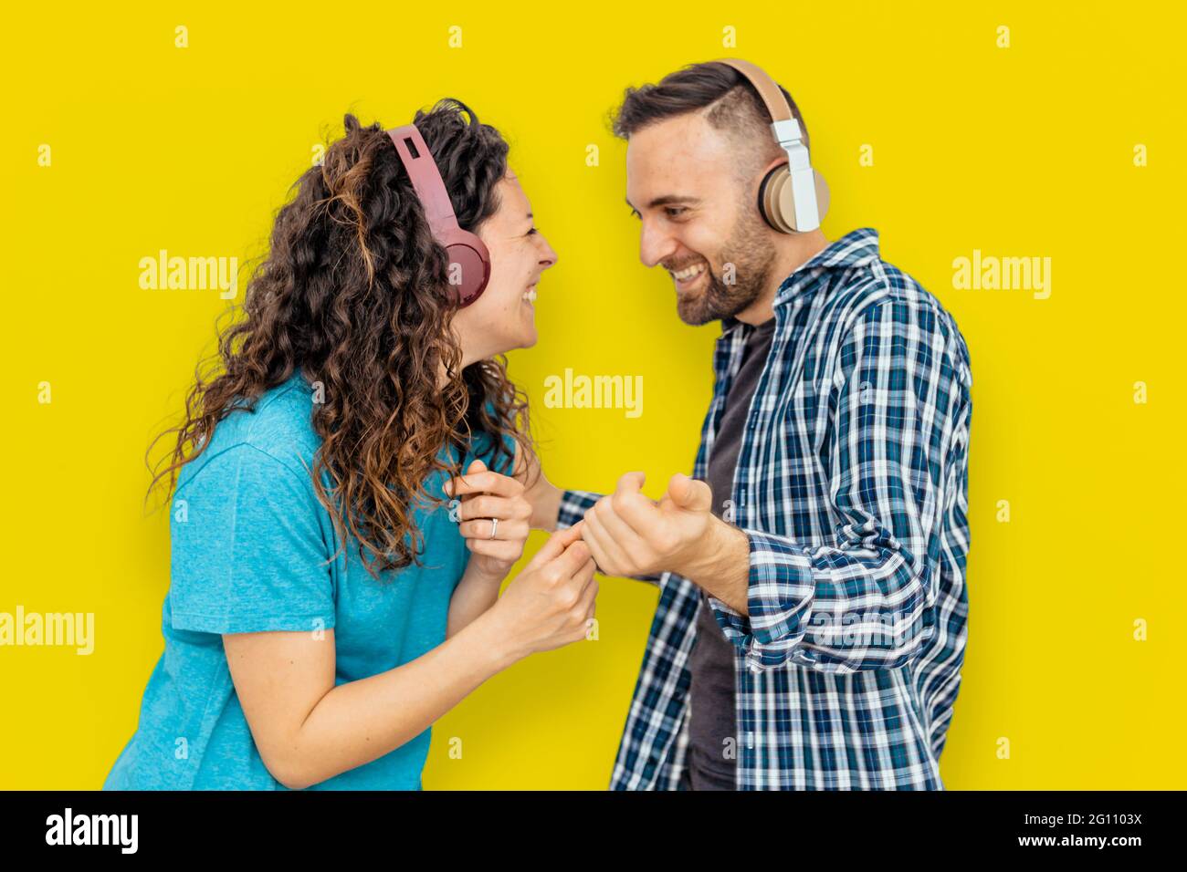 Couple on yellow colored background is having fun and dancing listening ...