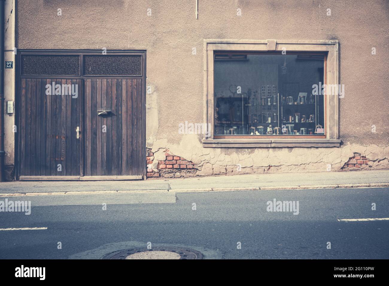 Old, gray building with a big window and vintage door near the asphalt ...
