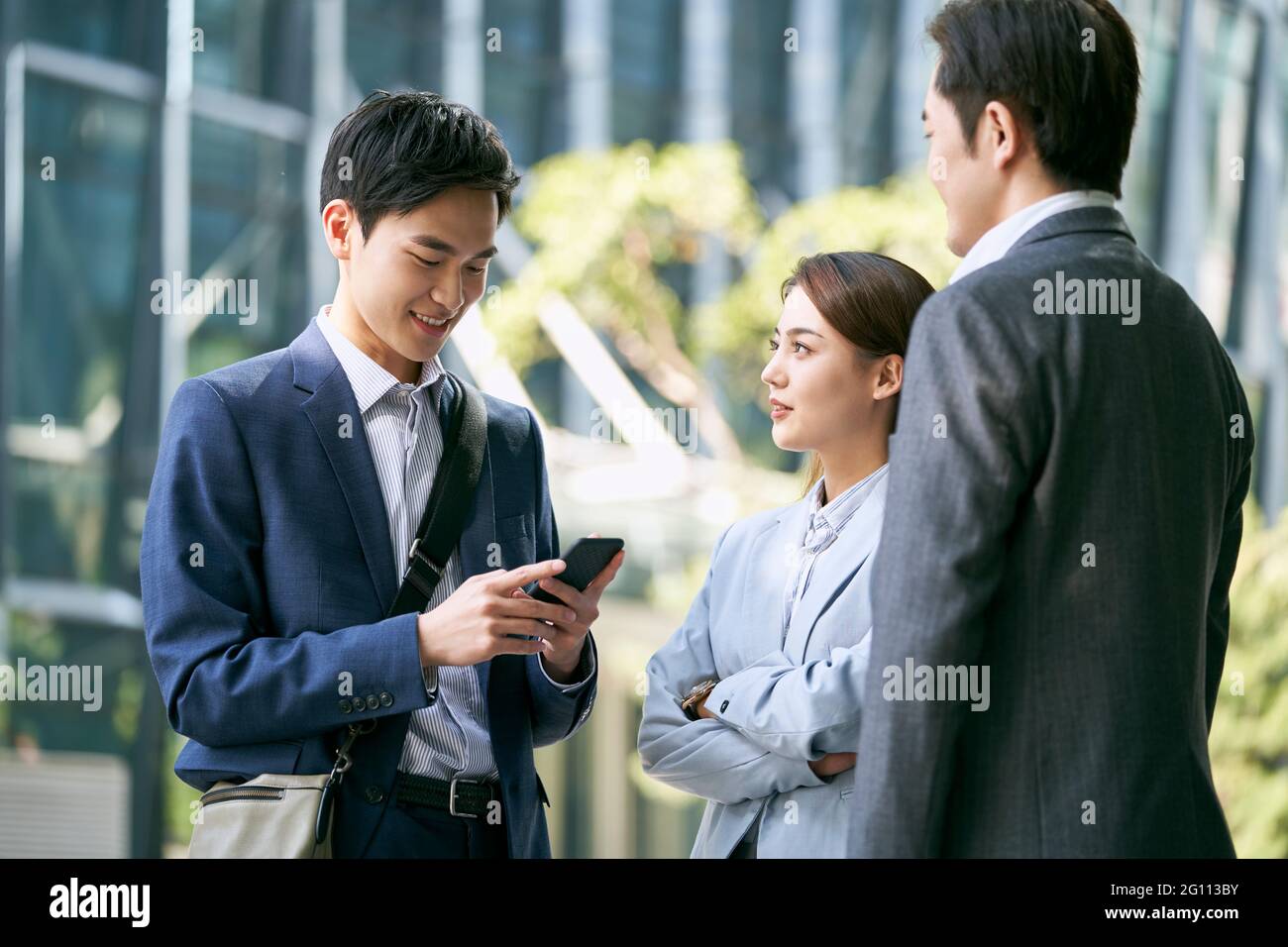 three asian business associates chatting in the street of downtown ...