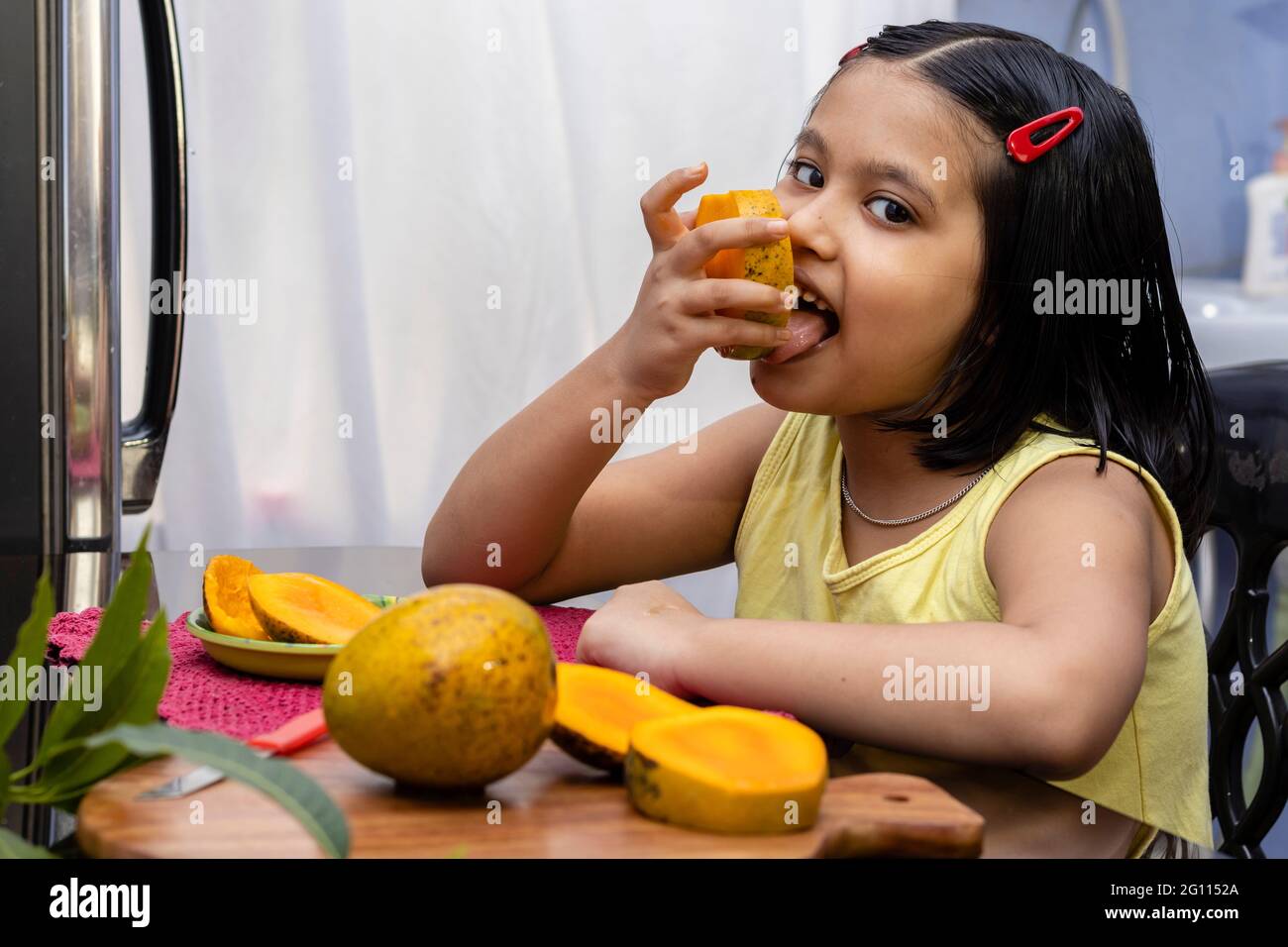 An Indian girl child eating mango and smiling at the camera sitting ...