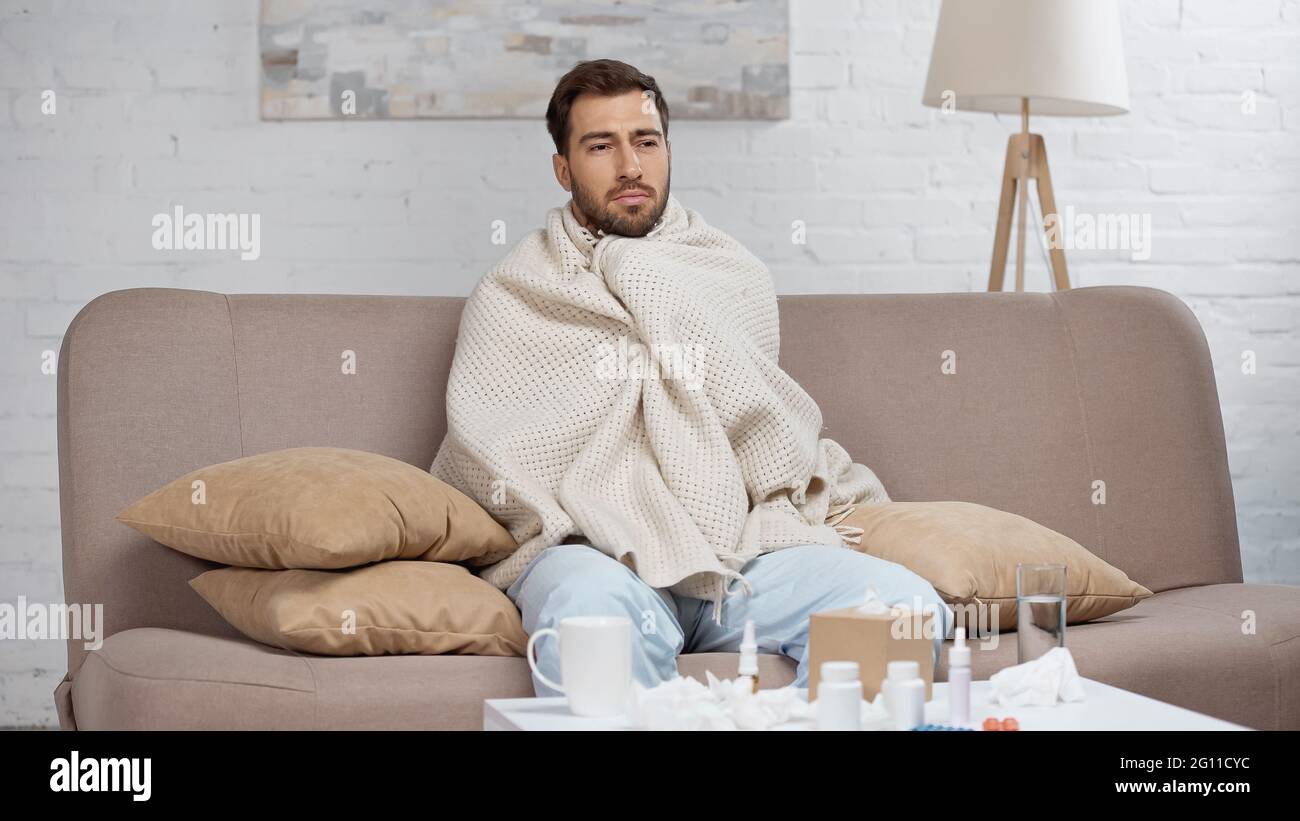sick man wrapped in blanket sitting on sofa in living room Stock Photo ...