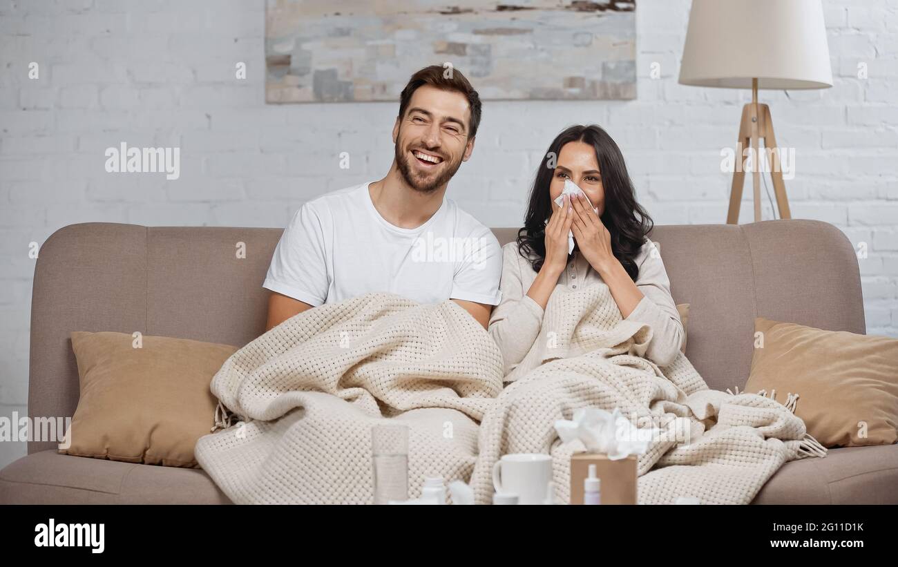 bearded man smiling near sick girlfriend sneezing in tissue Stock Photo ...
