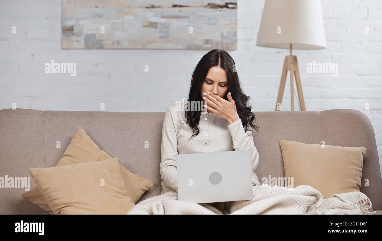 sick brunette freelancer with running nose using laptop in living room ...