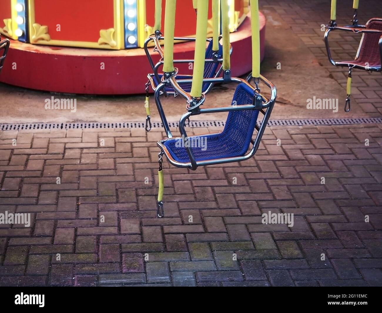 Empty hanging seats of a glowing carousel over paving slabs on dark ...