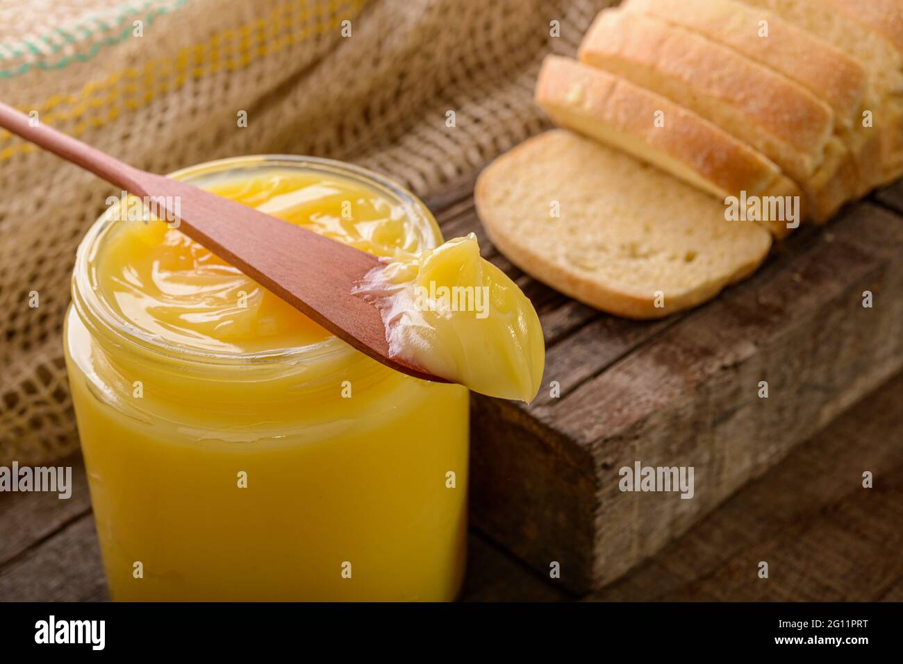 Ghee butter in glass jar with wooden spatula and sliced bread on wooden ...
