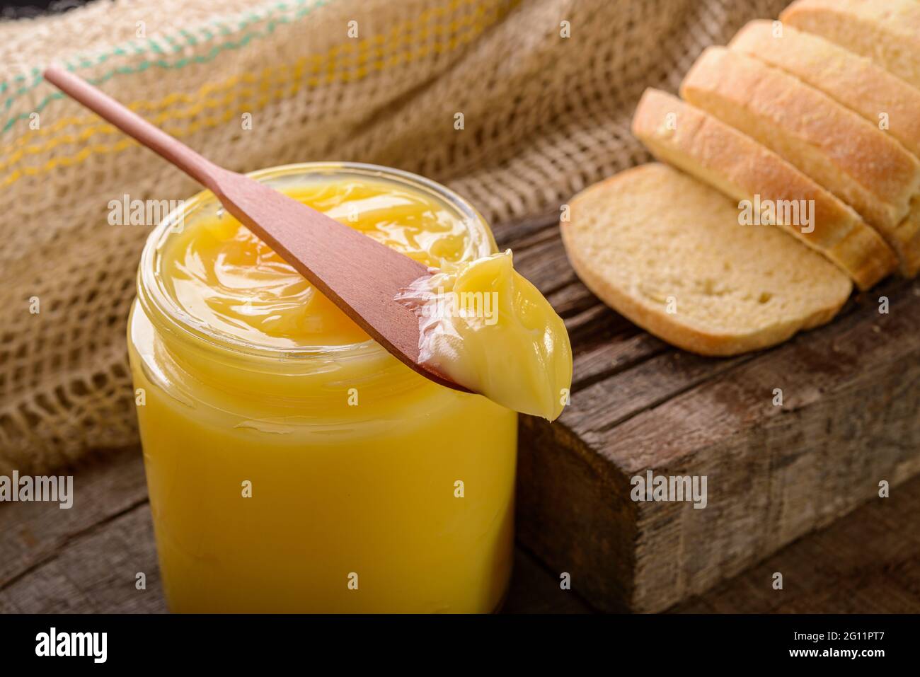 Ghee butter in glass jar with wooden spatula and sliced bread on wooden ...