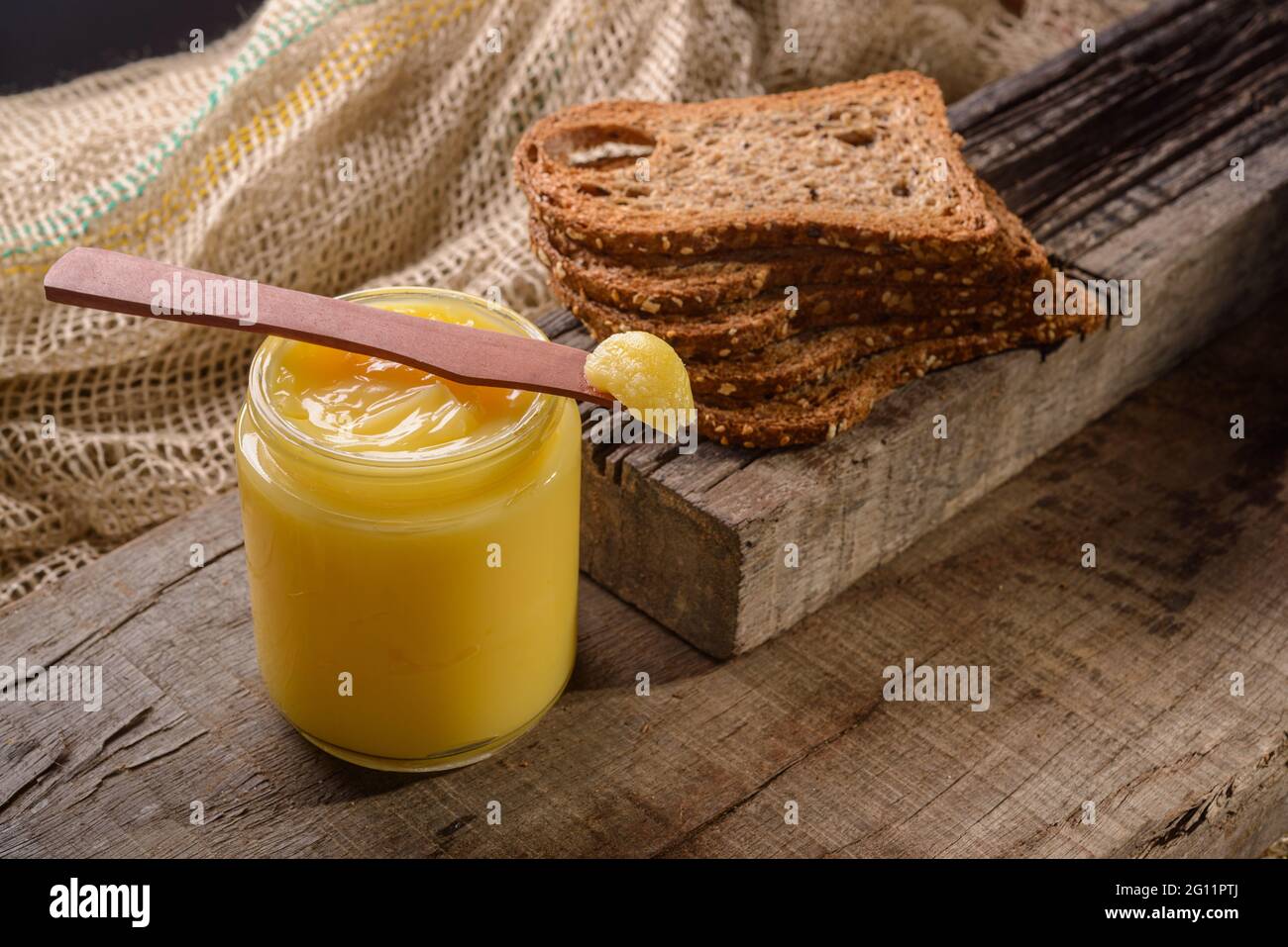 Ghee butter in glass jar with wooden spatula and sliced bread on wooden ...
