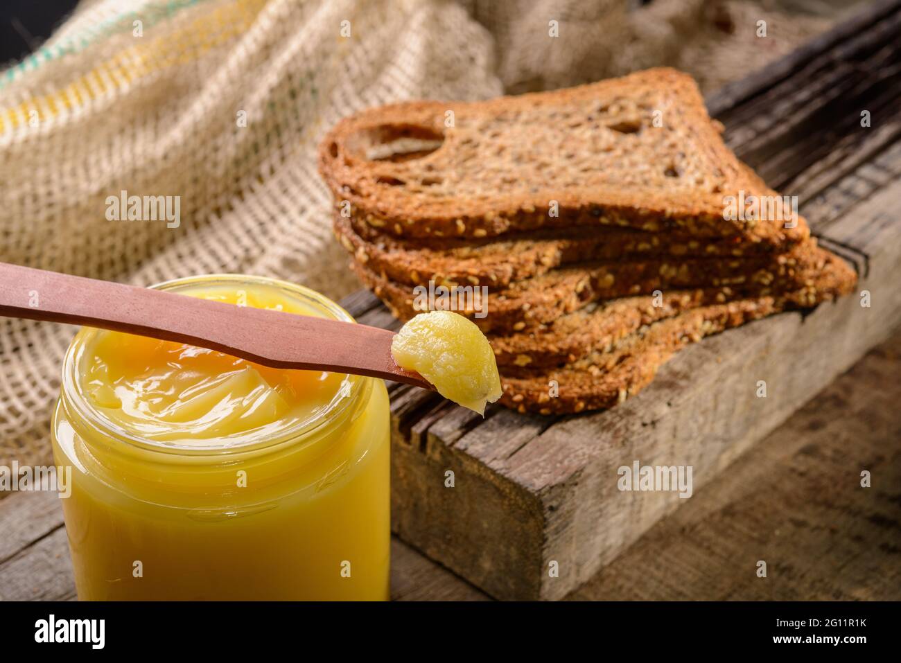 Ghee butter in glass jar with wooden spatula and sliced bread on wooden ...