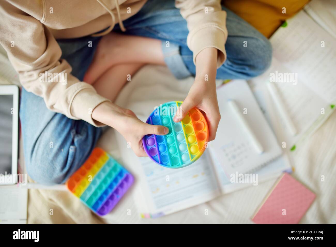 Teenage girl playing with rainbow pop-it fidget toy while studying at ...