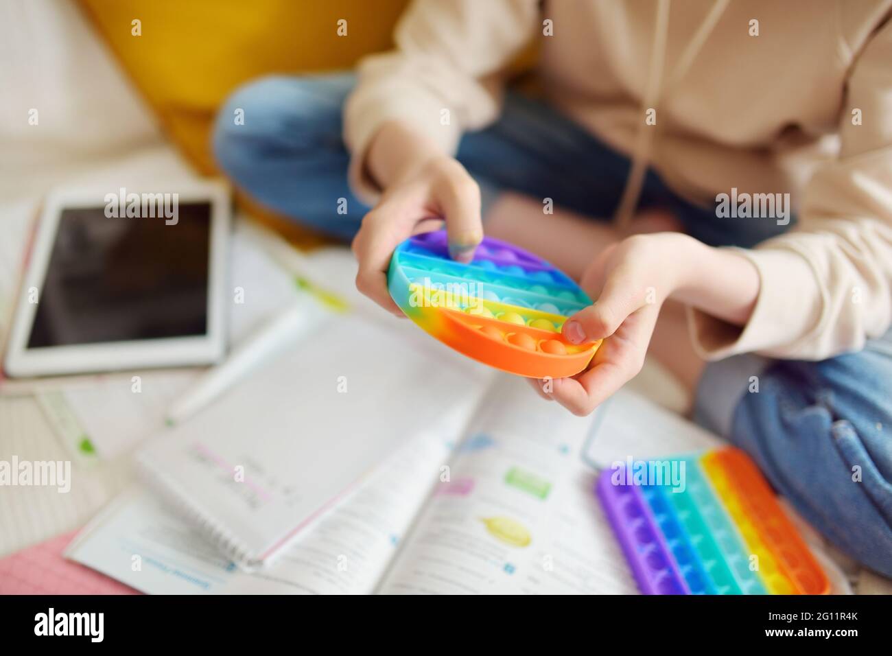 Teenage girl playing with rainbow pop-it fidget toy while studying at ...