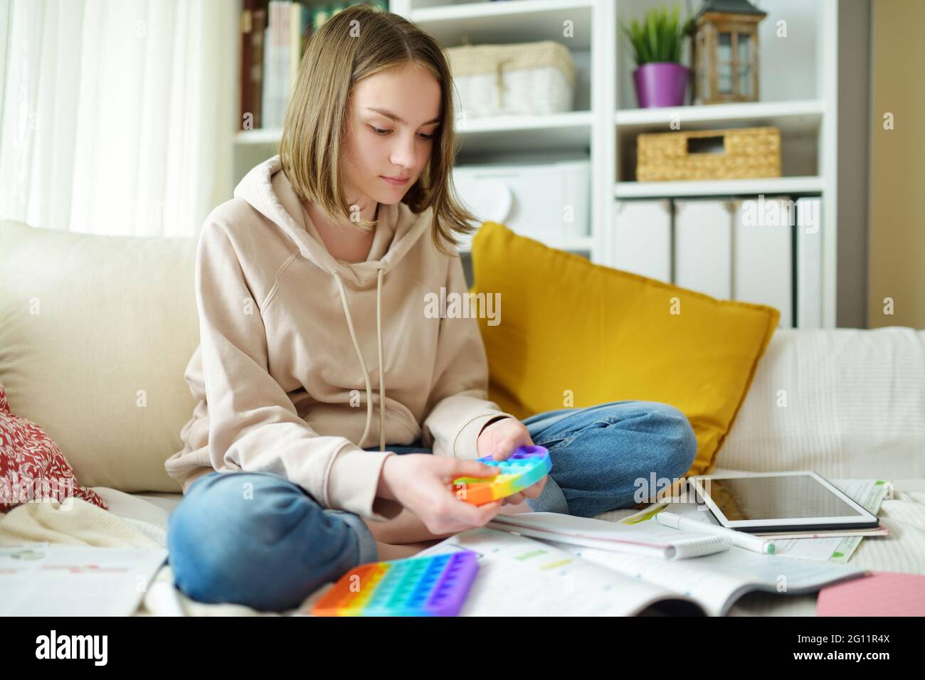 Teenage girl playing with rainbow pop-it fidget toy while studying at ...