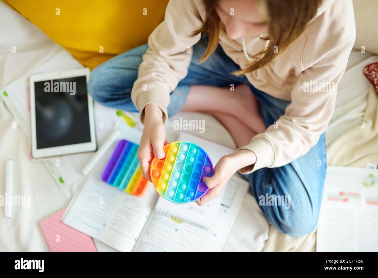 Teenage girl playing with rainbow pop-it fidget toy while studying at ...
