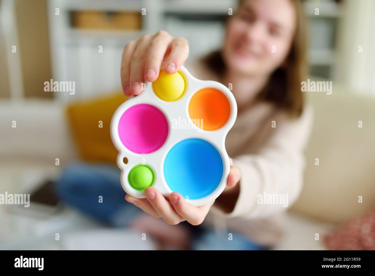 Teenage girl playing with rainbow pop-it fidget toy while studying at ...