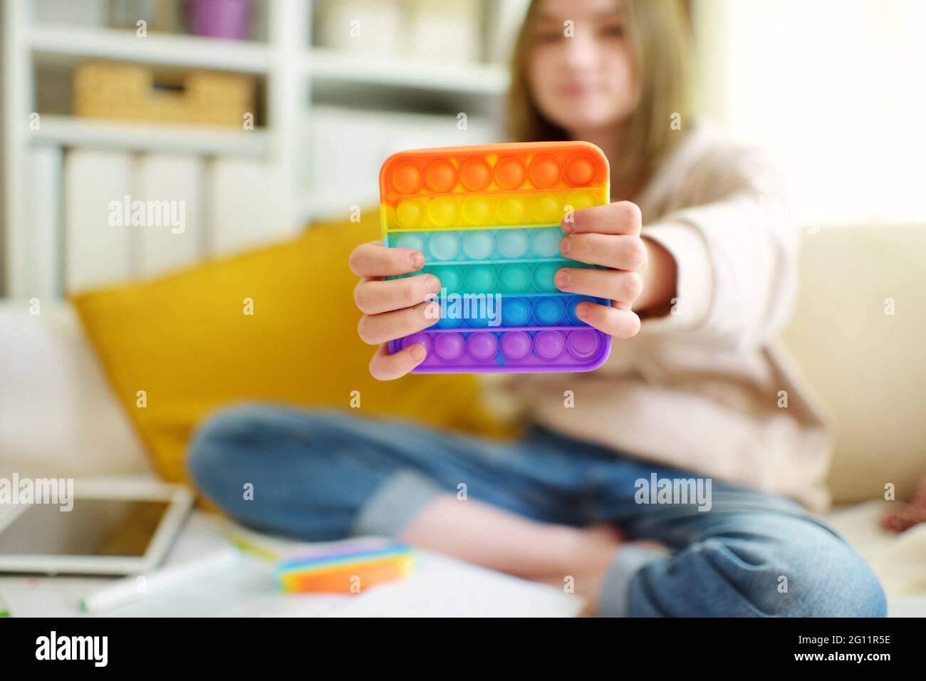 Teenage girl playing with rainbow pop-it fidget toy while studying at ...