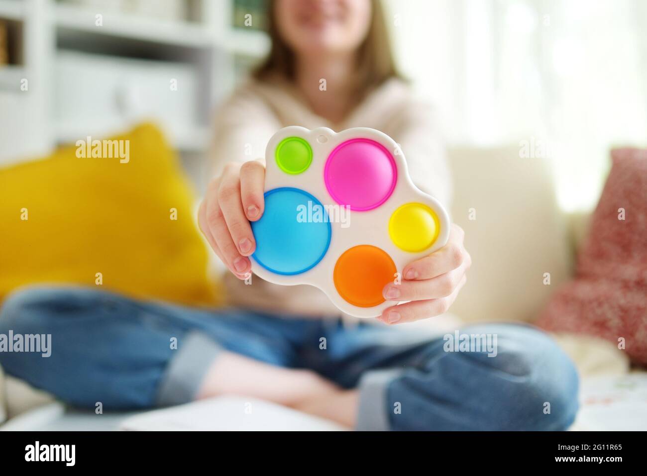 Teenage girl playing with rainbow pop-it fidget toy while studying at ...