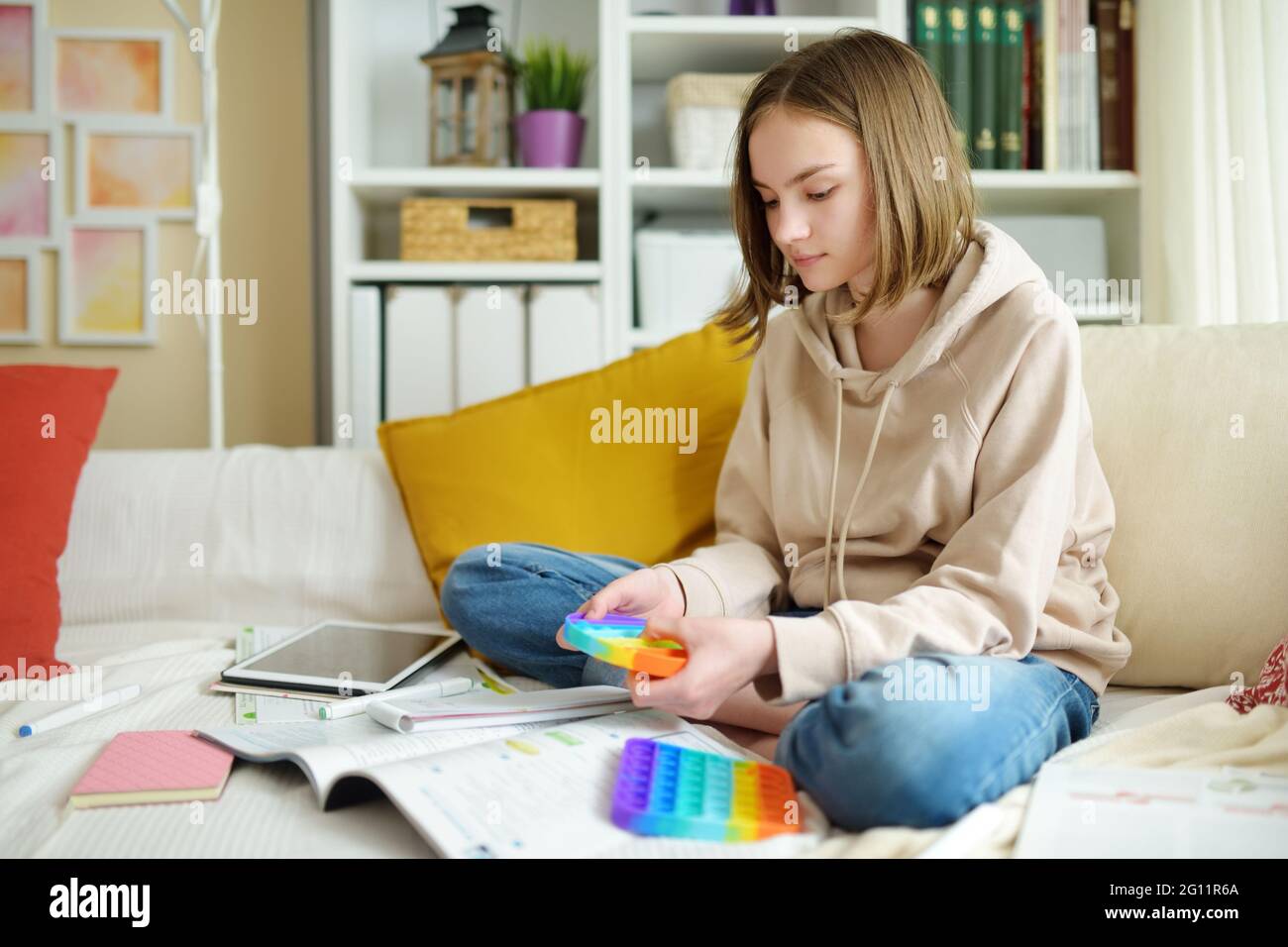 Teenage girl playing with rainbow pop-it fidget toy while studying at ...