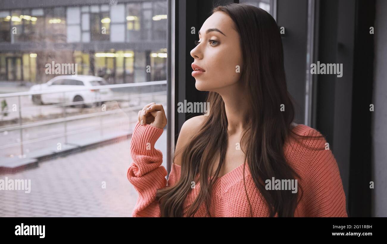 tense young adult woman standing near window in modern loft Stock Photo ...