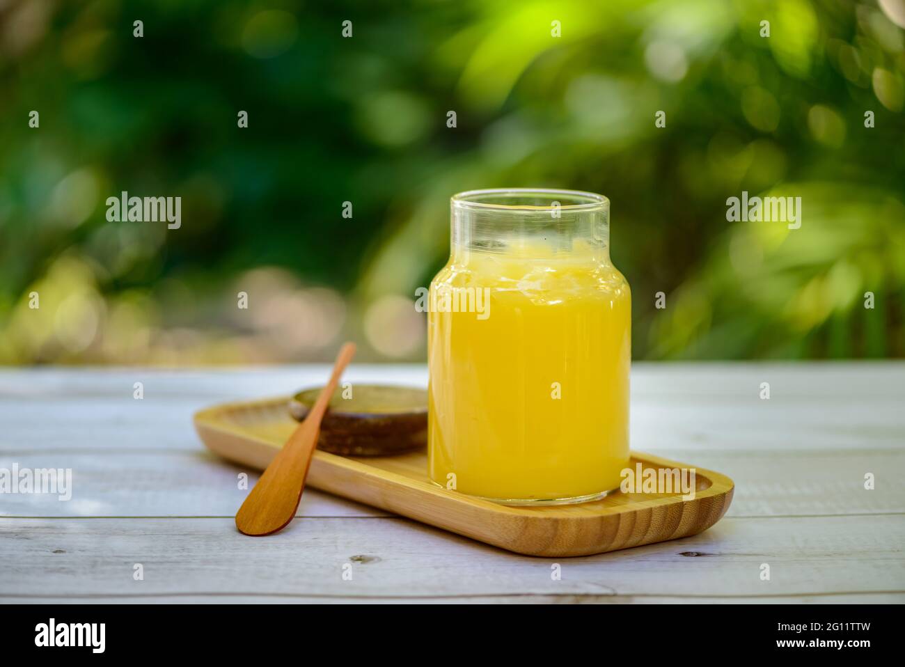 Ghee butter in glass jar with wooden spatula on white wooden table with ...