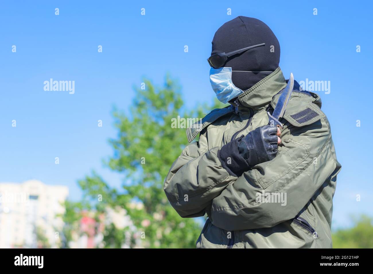 Modern dangerous and armed criminal in balaclava and medical mask among ...