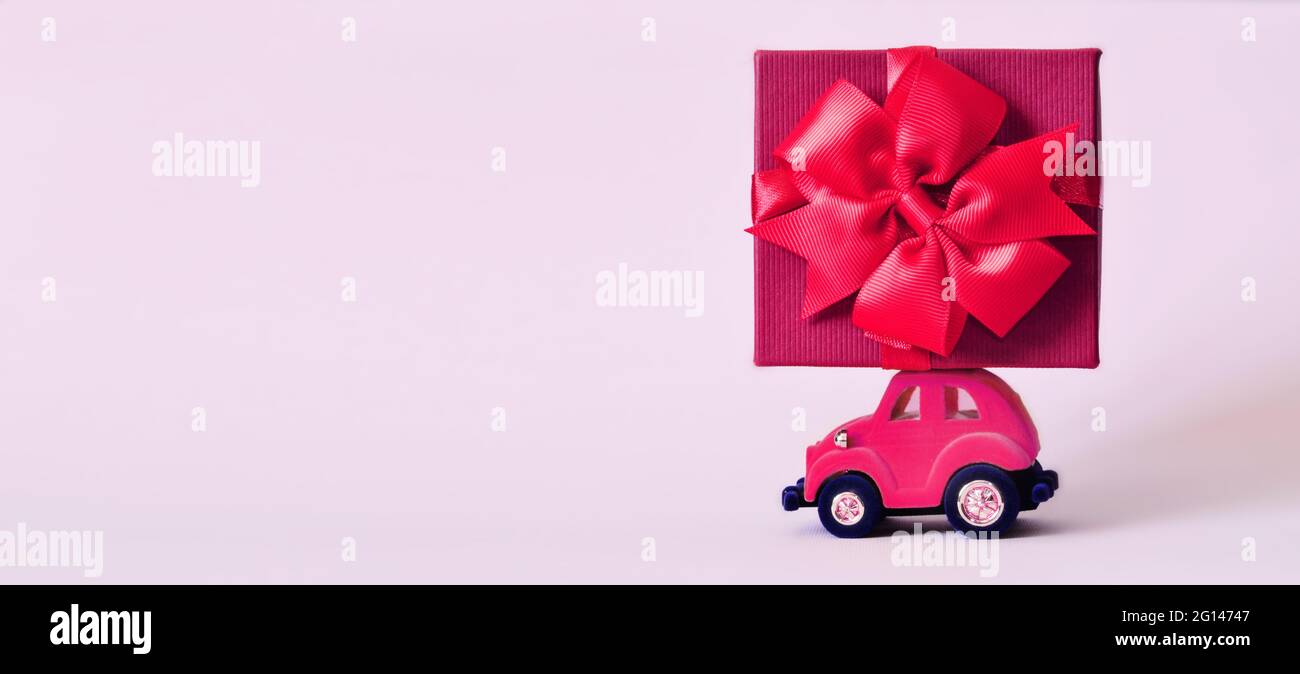 Pink toy retro car with gift box on a roof on pink background. Copy ...