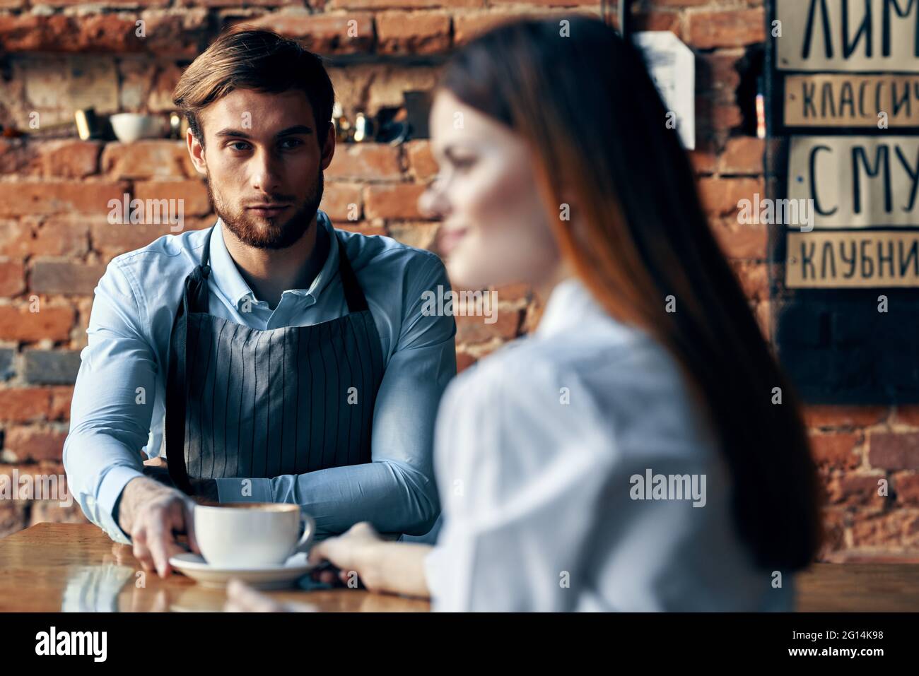 happy woman with a cup of coffee and male bartender in the apron at the ...