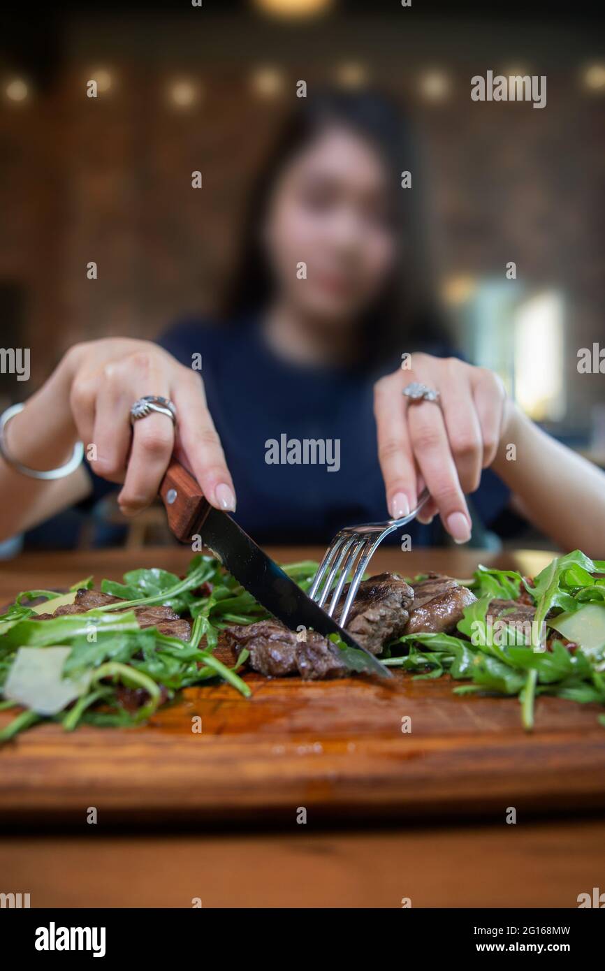 Girl eats steak with greens on a wooden board Stock Photo - Alamy