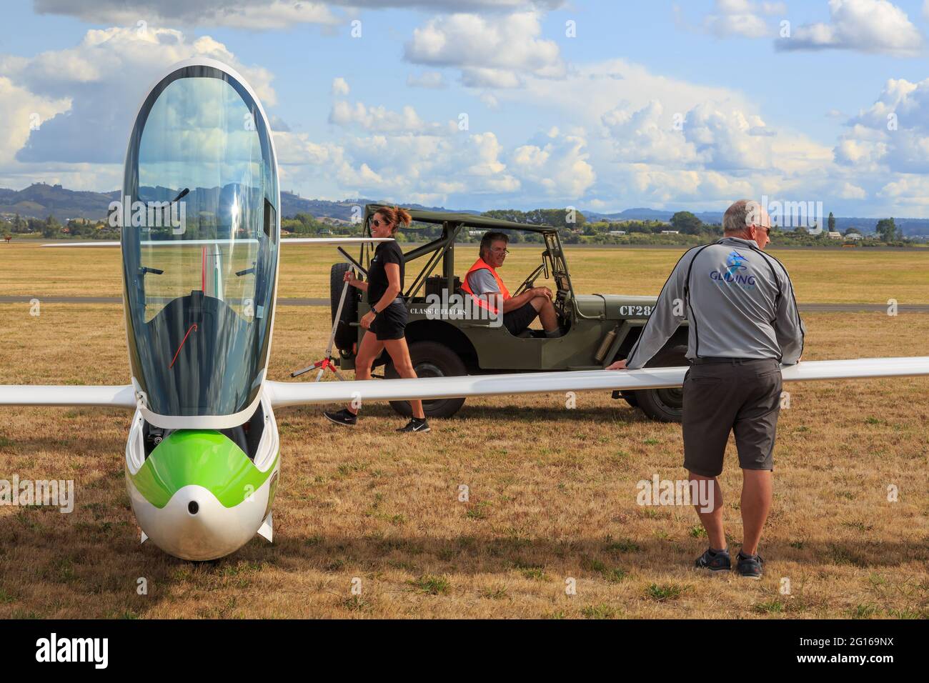 A glider with its cockpit open on the ground. A jeep is passing by in ...