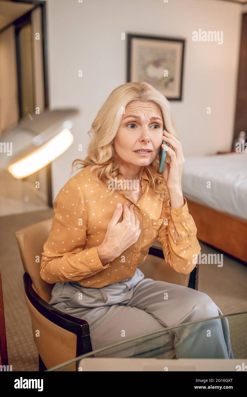 Blonde pretty woman sitting talking on the phone and looking stressed ...