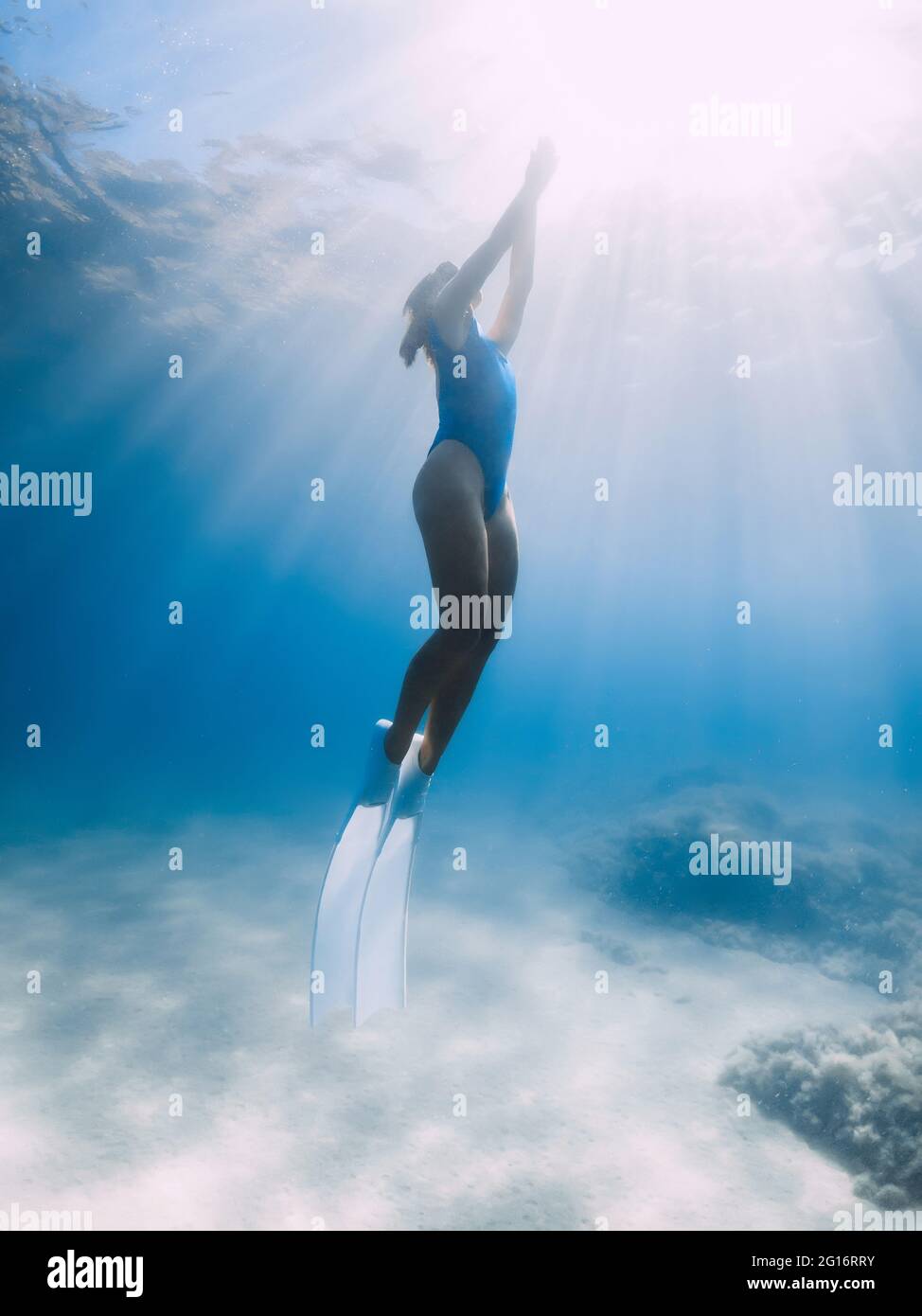 Female freediver with fins glide underwater in ocean with sunlight ...