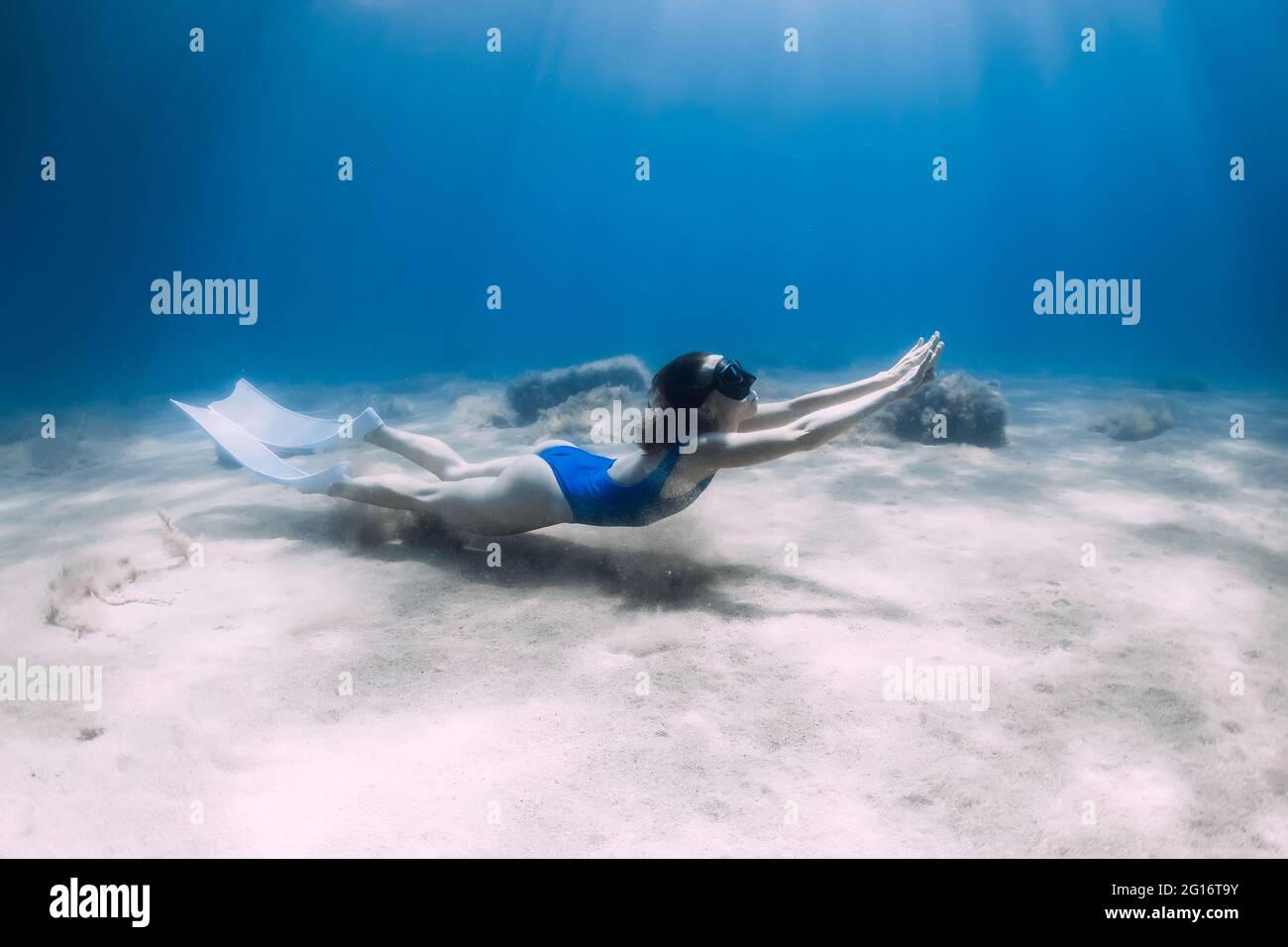 Female freediver with fins glide underwater in ocean with sunlight ...