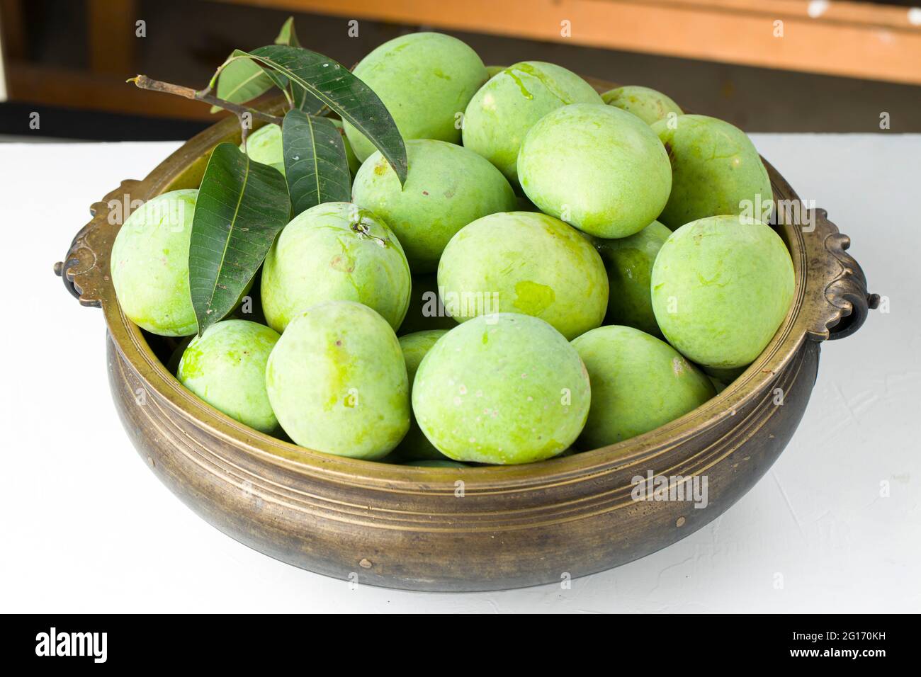 Raw mango or Green mango arranged in a traditional brass vessel with ...