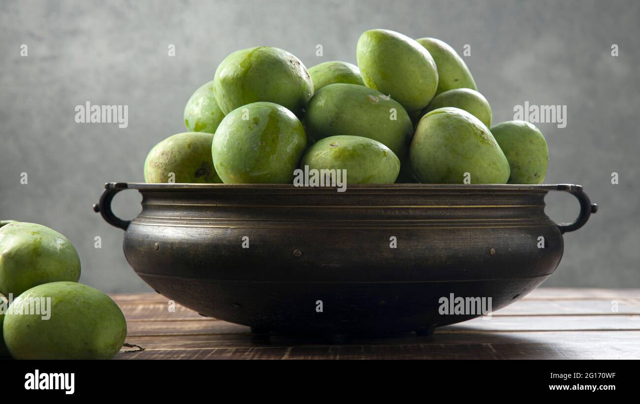 Raw Mango arranged traditionally in a brass vessel and bunch of green ...