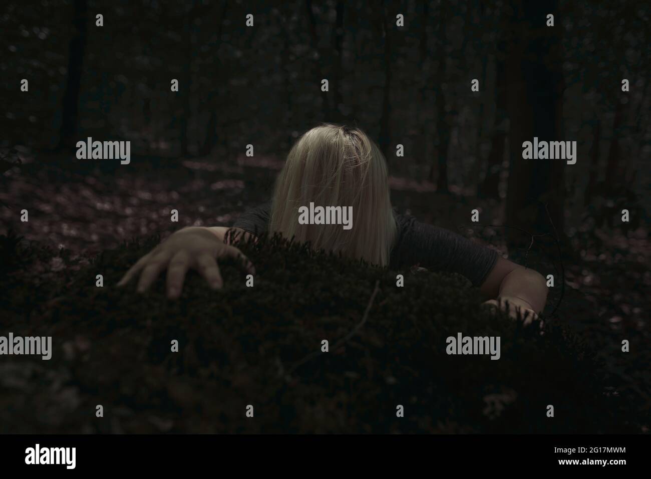 Scary woman crawling on the forest floor in dark, coming up behind tree ...