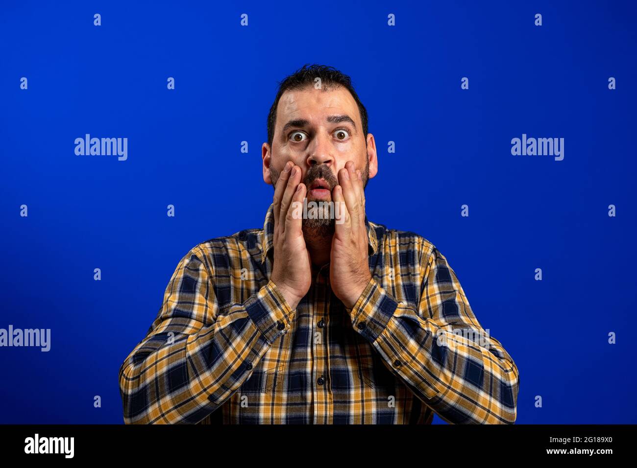 Scared bearded man with his hands on his face and wide eyes isolated on ...