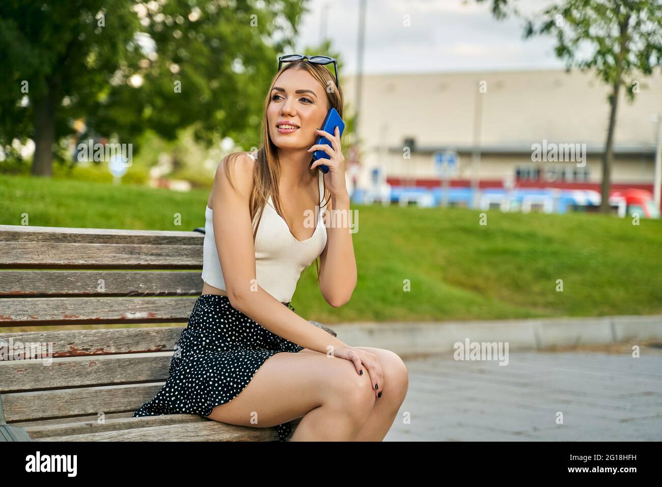 Happy girl calling on cell phone looking away sitting on a bench in the ...