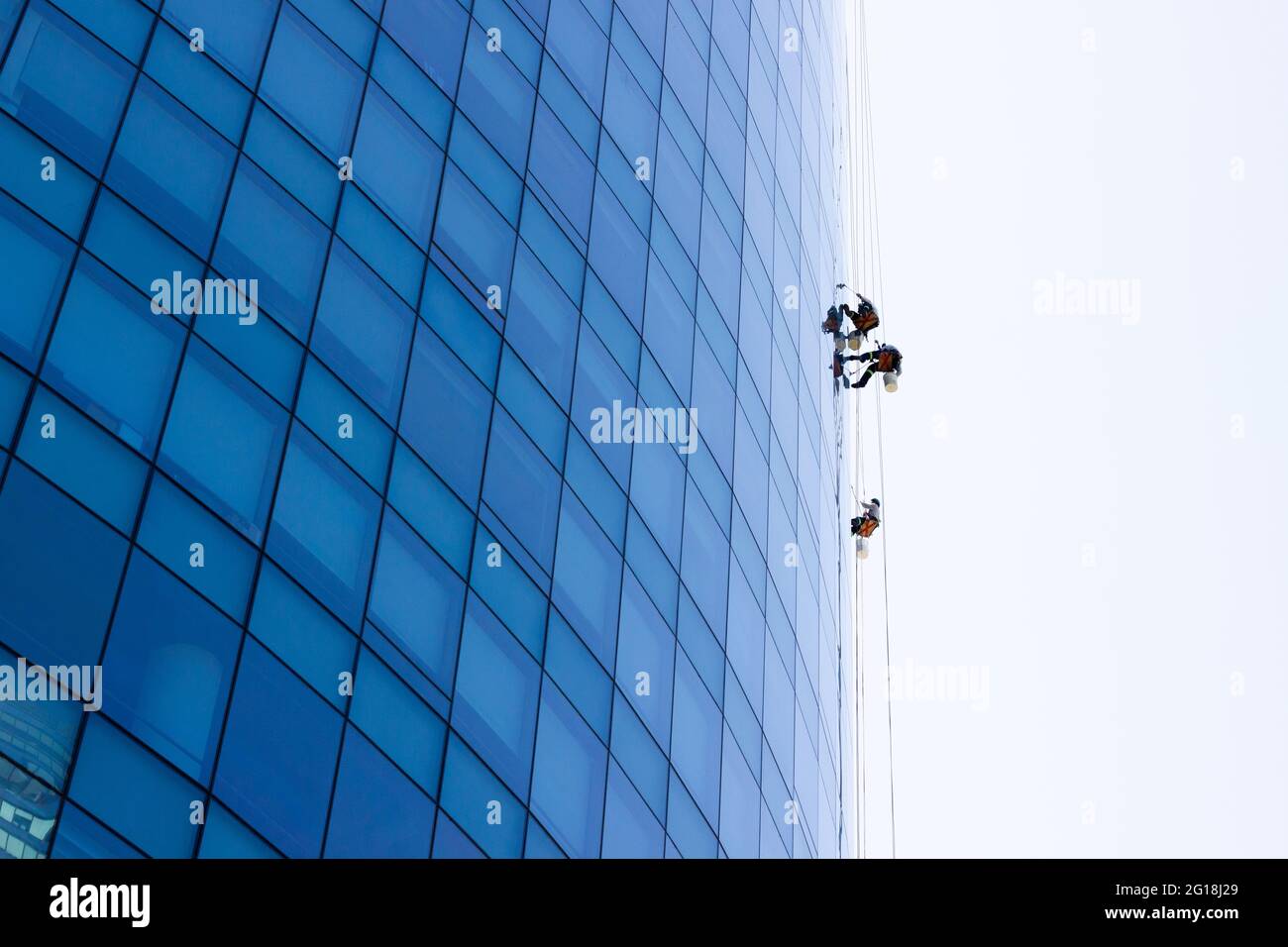 Window washers hanging outside blue glass modern building. Risky job ...